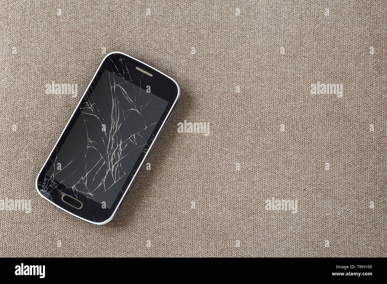 Black old cellphone with cracked screen on light cloth copy space ...