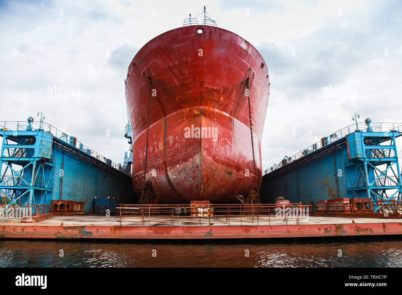Huge red tanker is under repairing in blue dry dock. Front view ...