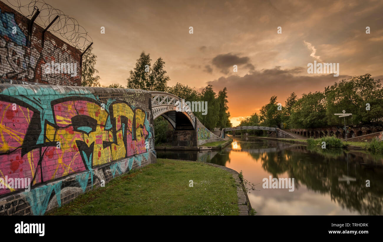 Spectacular sunset over a calm canal, with a graffiti covered bridge in ...