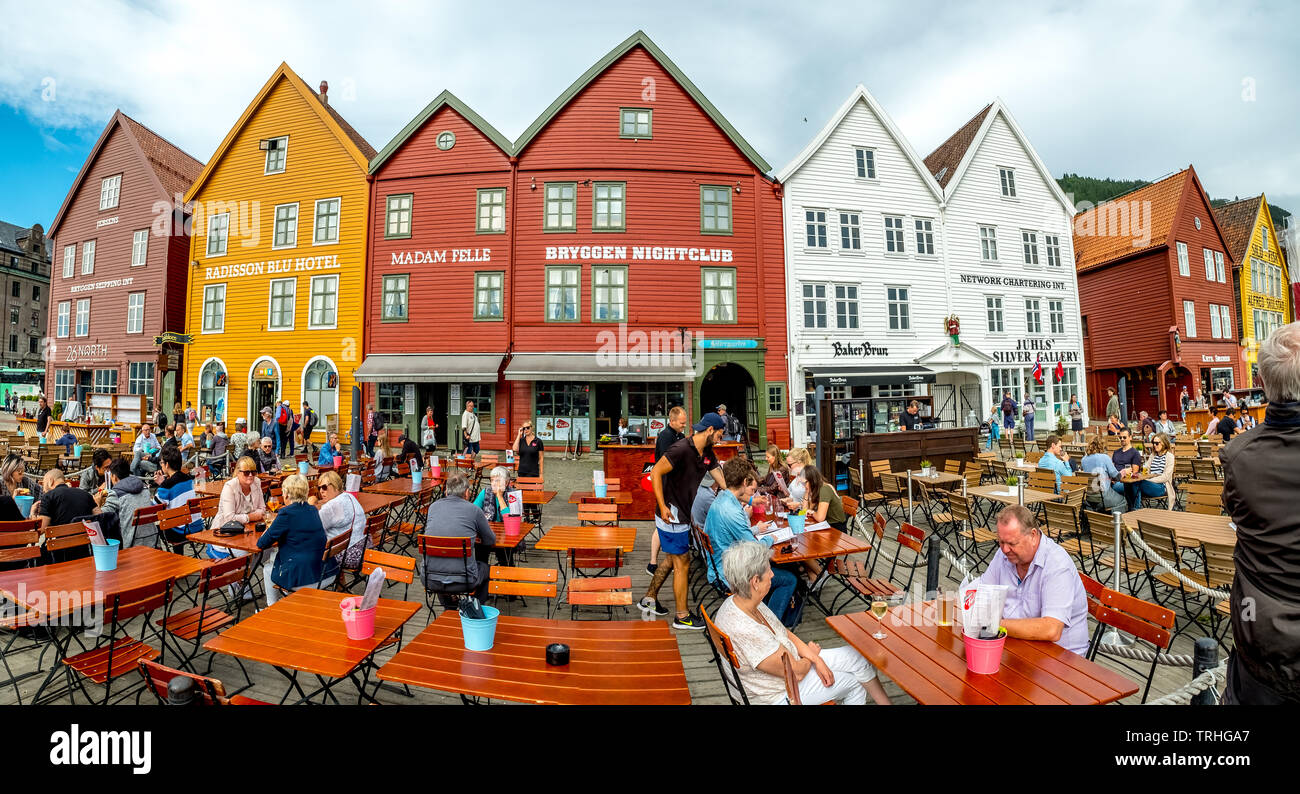 Tourists sit at tables against the historic backdrop of colorful wooden ...
