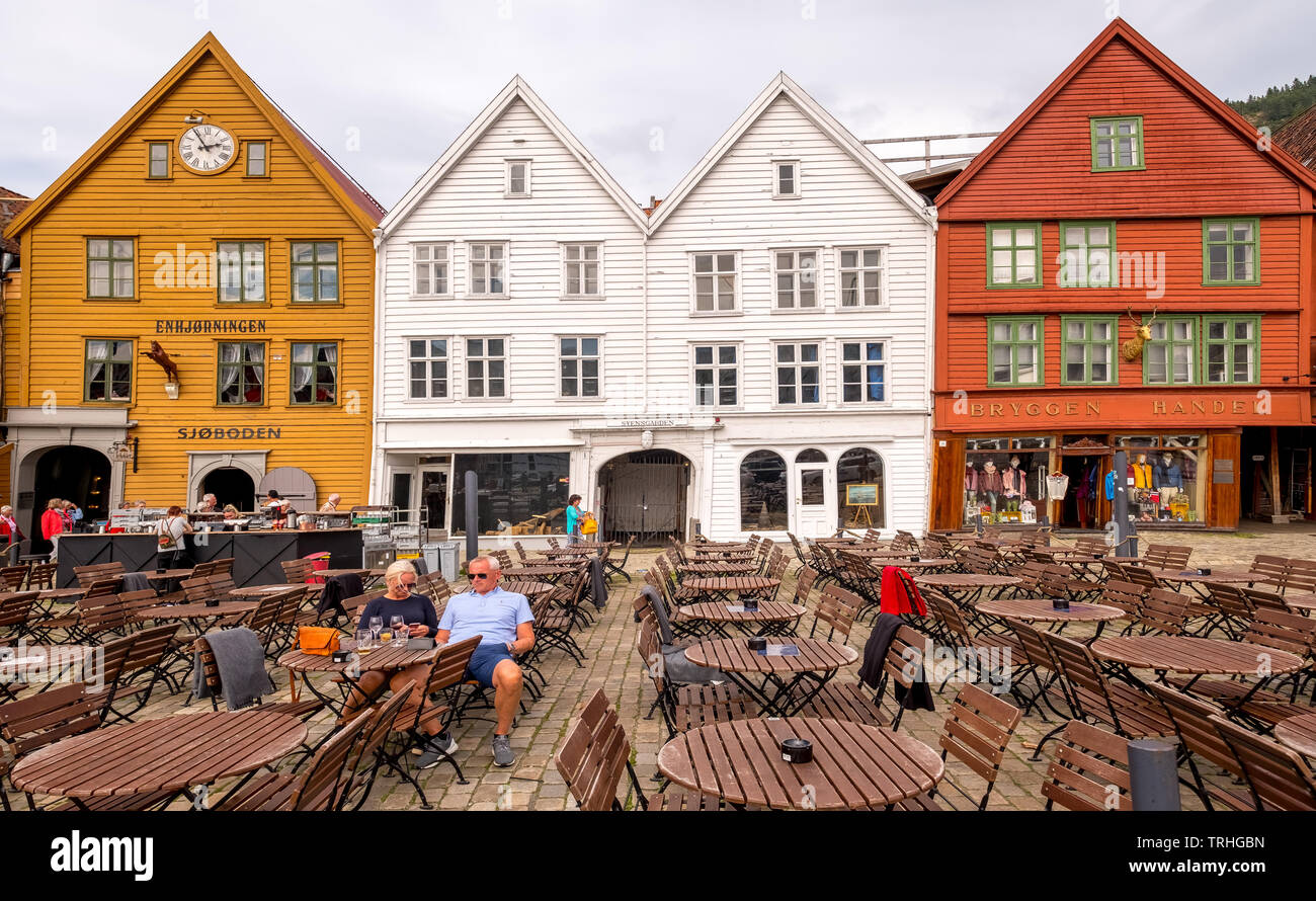 Tourists sit at tables against the historic backdrop of colorful wooden ...