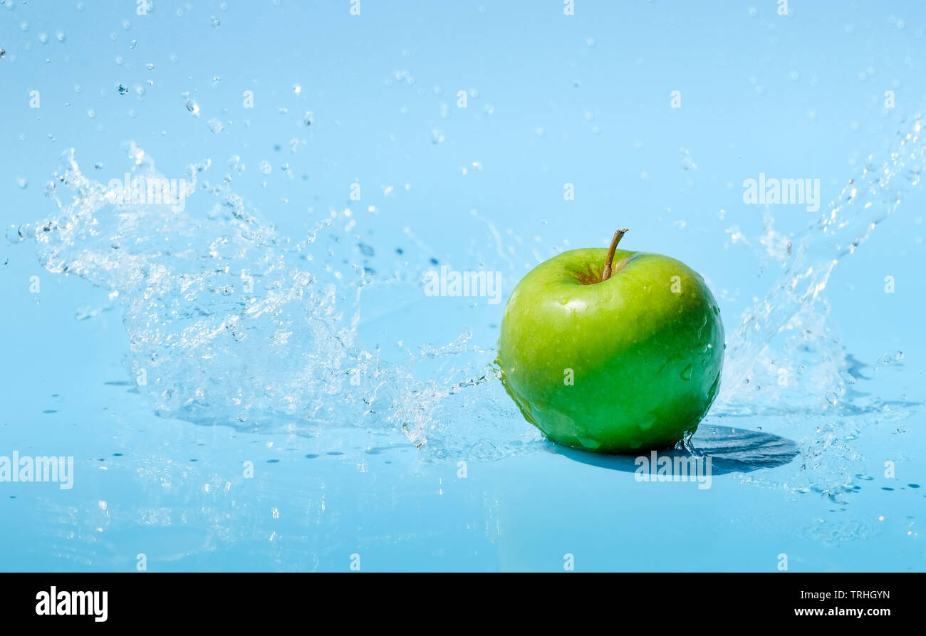 Green apple in water splash on blue background Stock Photo - Alamy