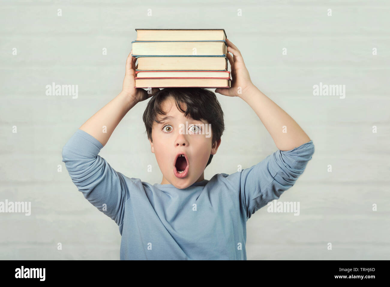 surprised child with books on head on brick background Stock Photo - Alamy