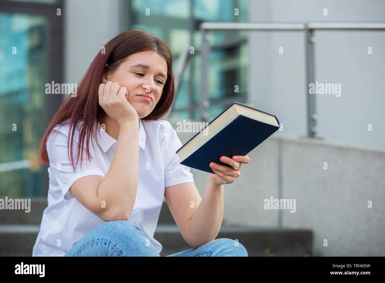 Demotivated student sitting on campus stairs trying to study looking to ...