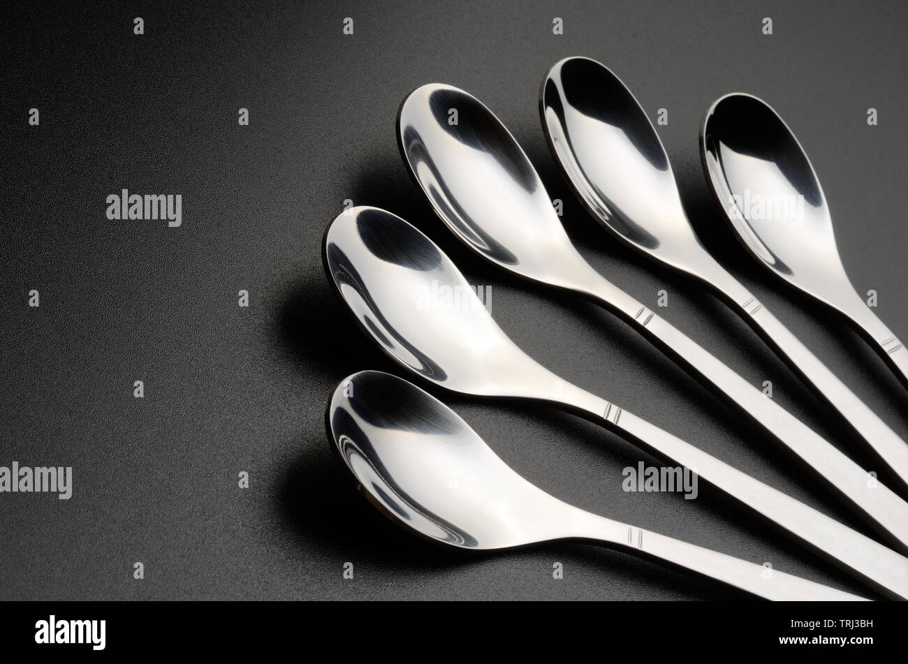 Teaspoons lined in a row on a black grained surface Stock Photo - Alamy