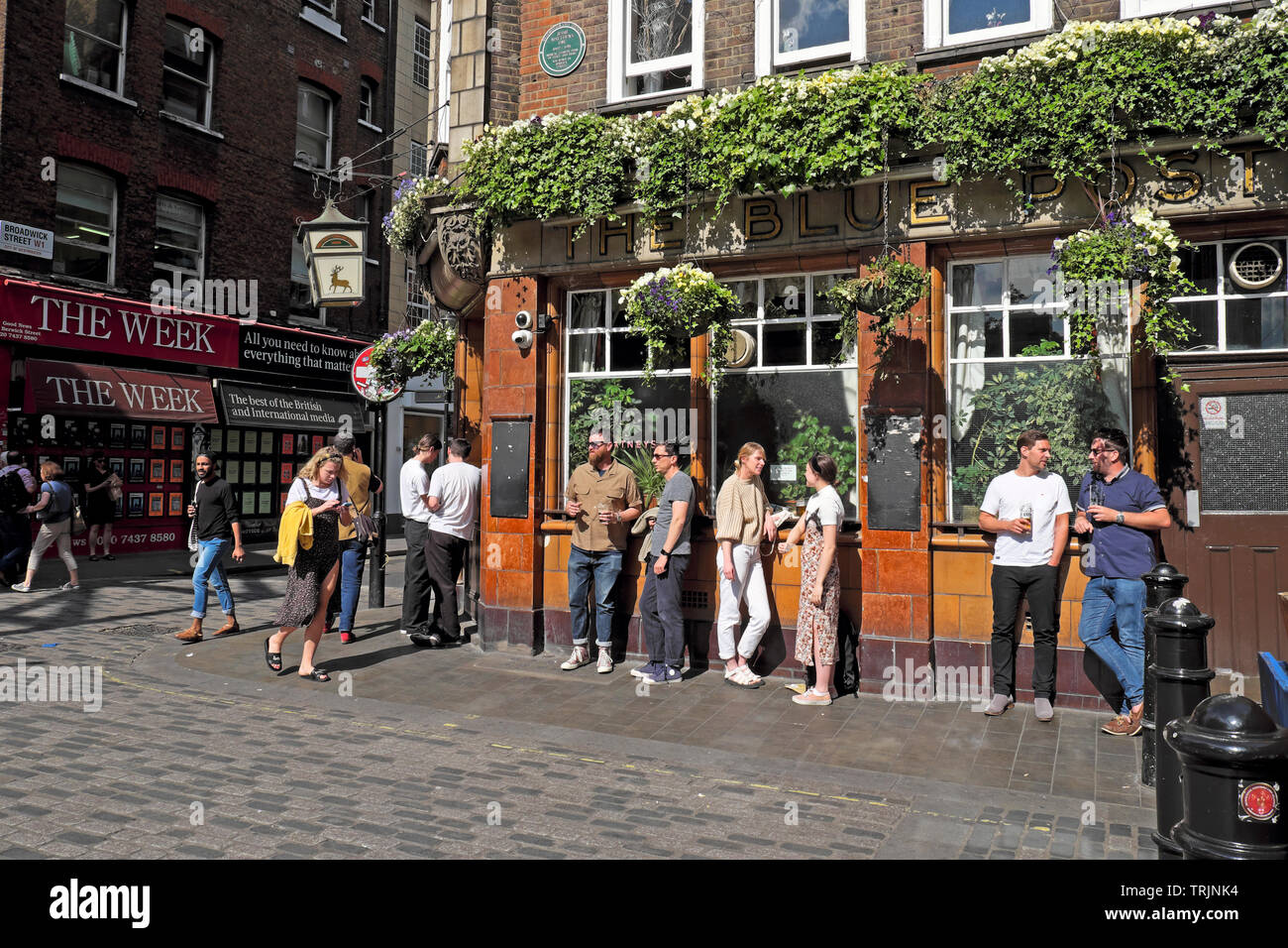Crowd of people standing drinking pints of beer outside the The Blue Posts pub in Berwick Street ...