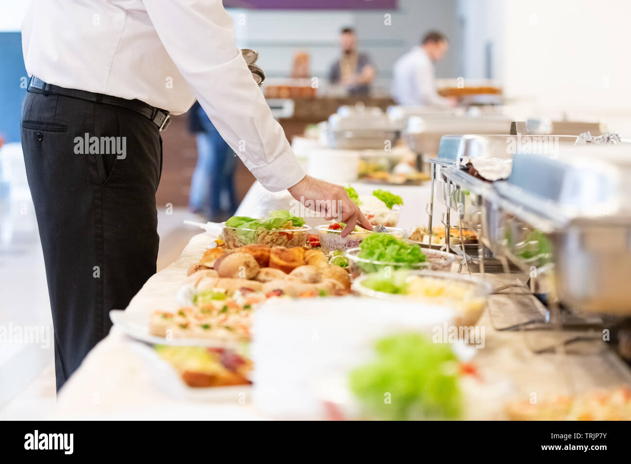 Waiter preparing buffet table with canapes and salads with vegetables ...