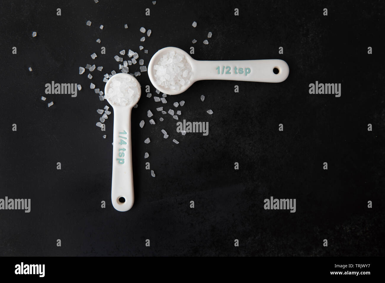Salt crystals in measuring spoons on black background Stock Photo - Alamy