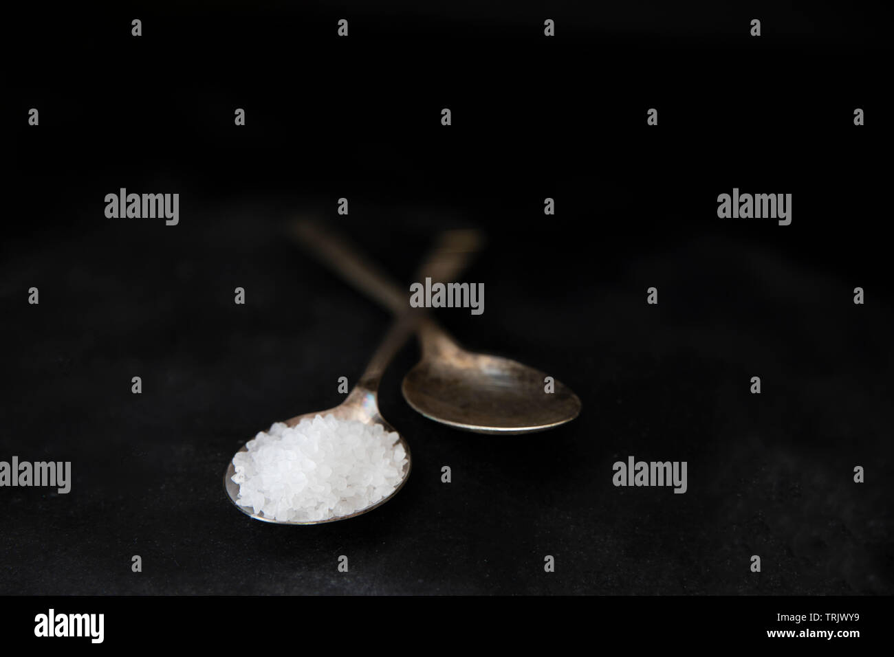 Salt crystals in metal spoons on black background Stock Photo - Alamy