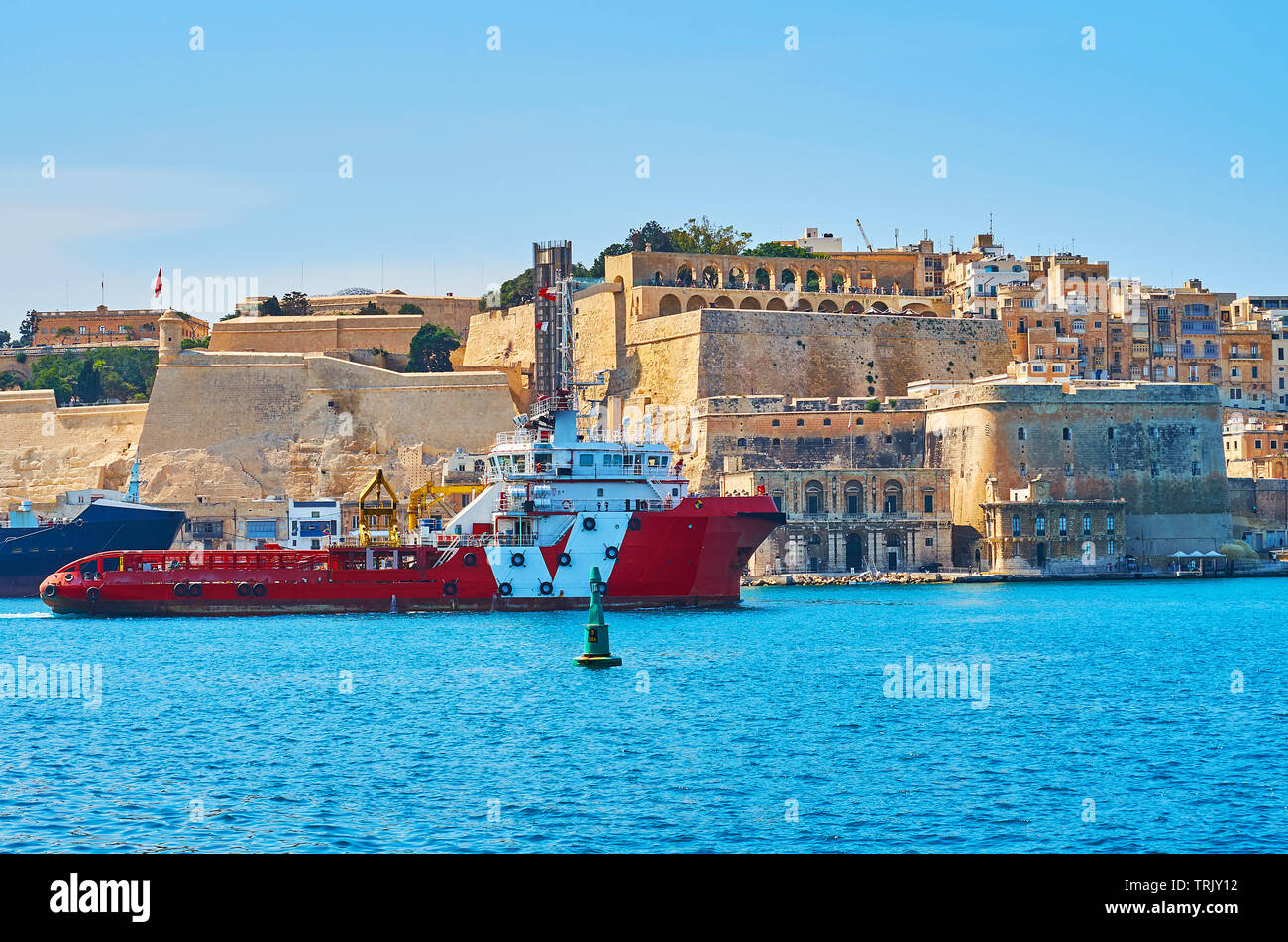The bright red cargo ships floats along Grand Harbor in front of the ...