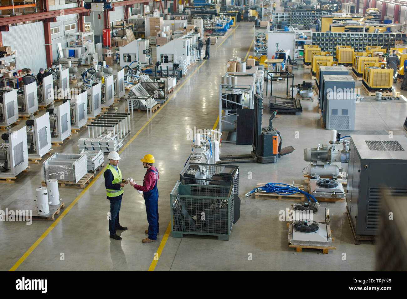 Factory warehouse overview with lined up product, and two colleagues ...