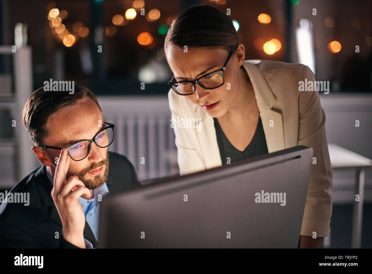 Portrait of man and woman working on computer late at night, looking at ...