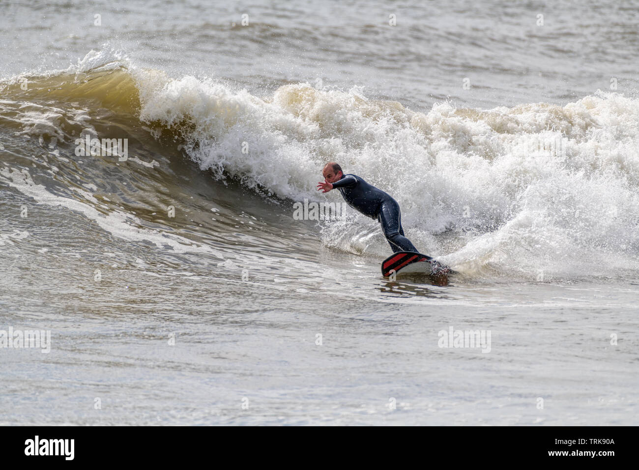 A middle aged man in wet suit surfing the waves at Rest Bay, Porthcawl ...