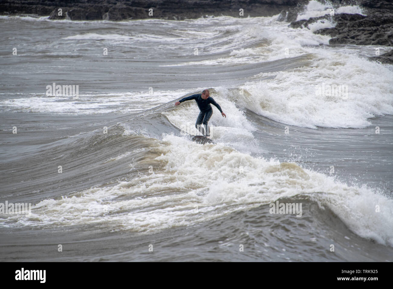A middle-aged surfer in wet suits hols his balance in tricky water ...