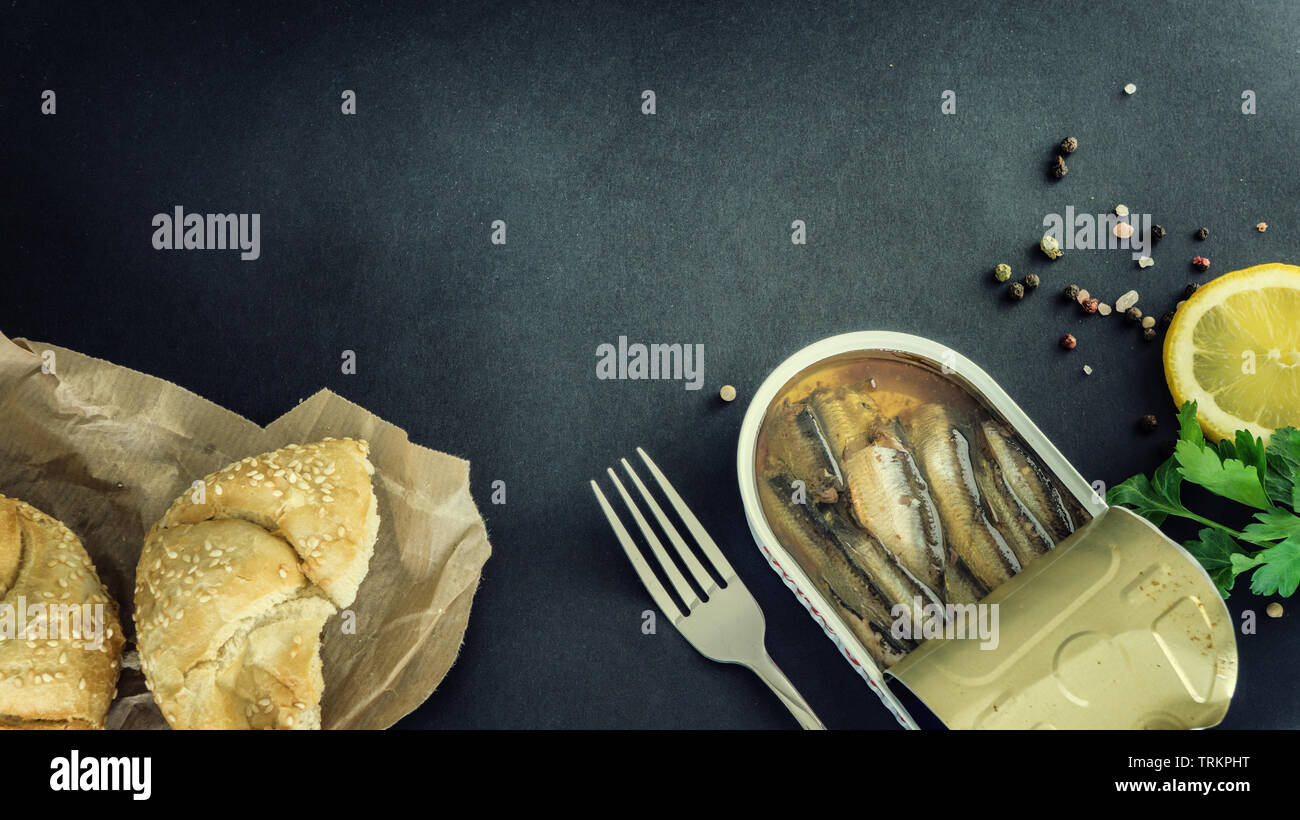 Opened fish can with lemon slice parsley and condiments on table bread ...