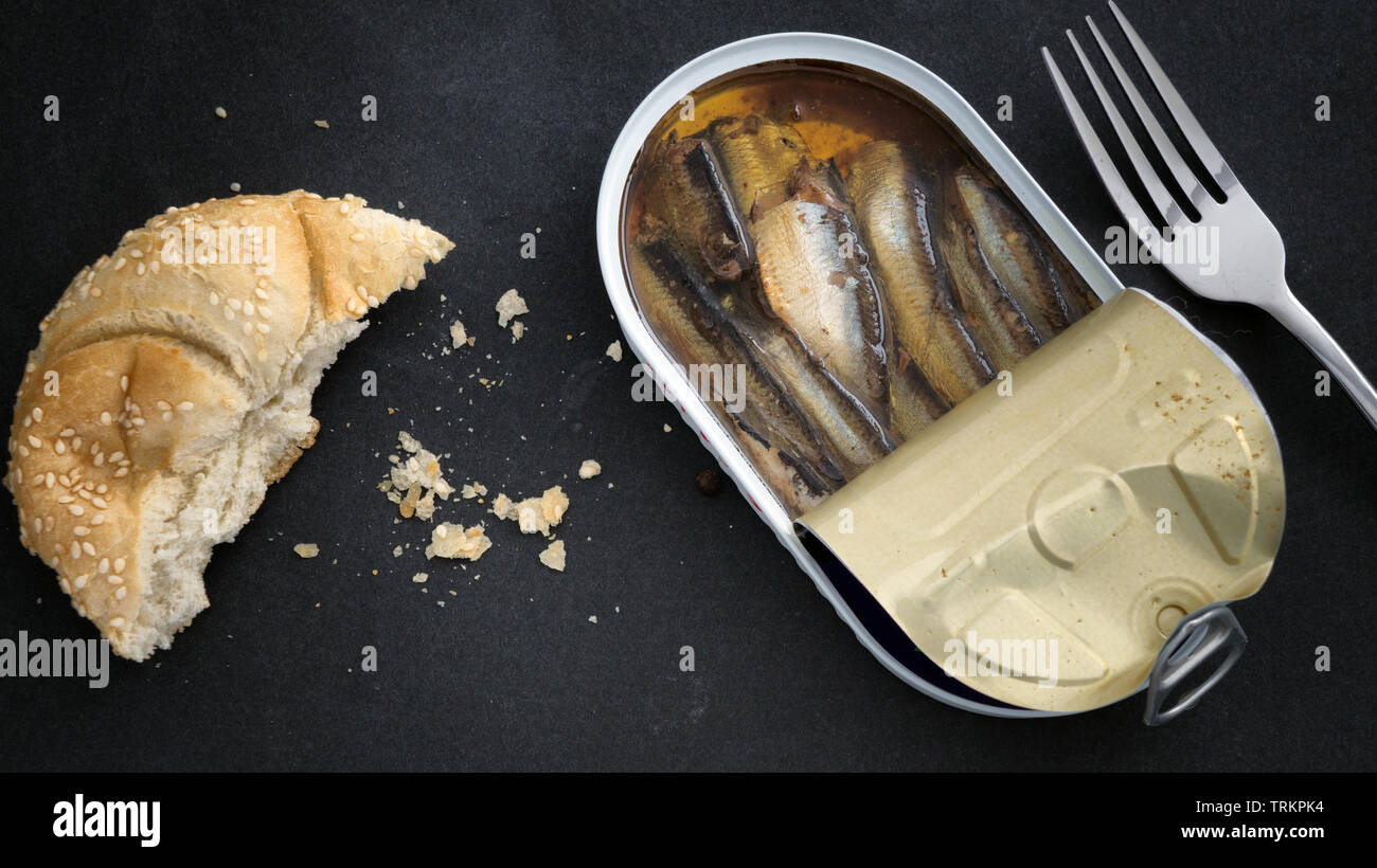 Opened fish can with lemon slice parsley and condiments on table bread ...