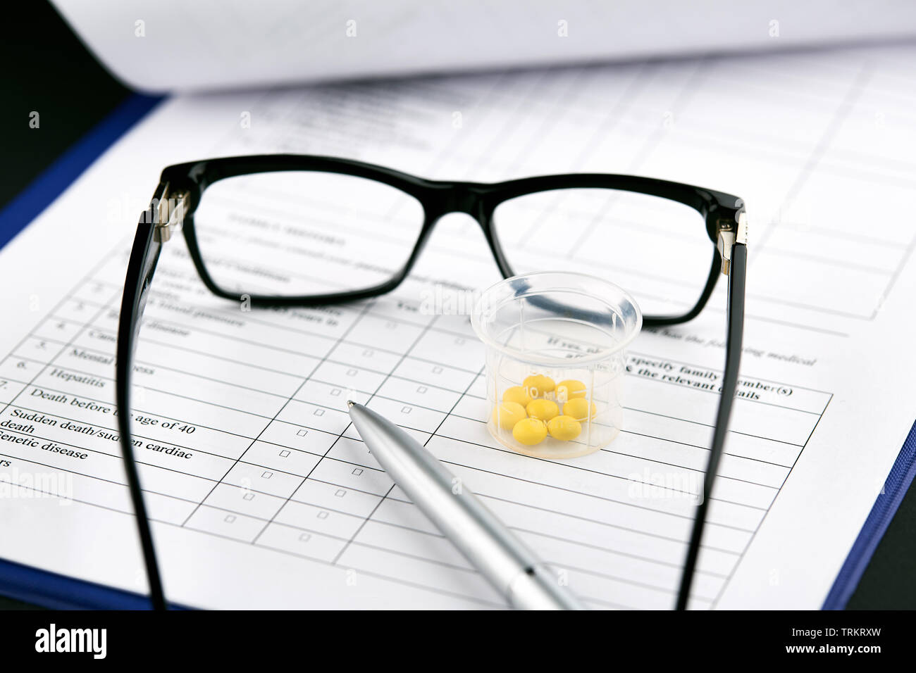 Glasses, yellow pills in graduated glass and pen on medical ...