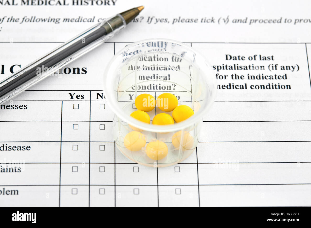 Yellow pills in graduated glass and pen on medical questionnaire form ...