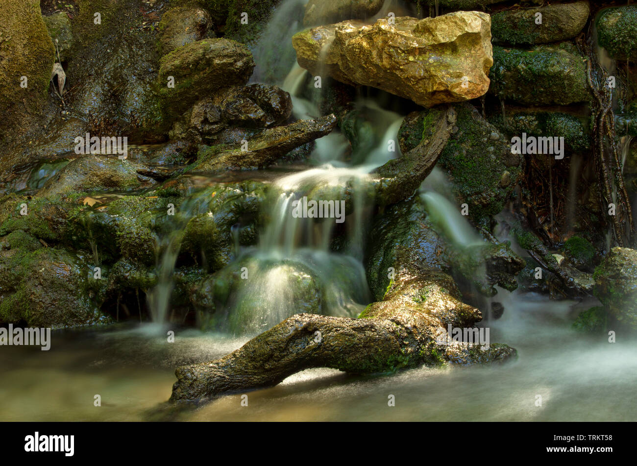 Small waterfall and stream of water among rocks and boulders and fallen ...
