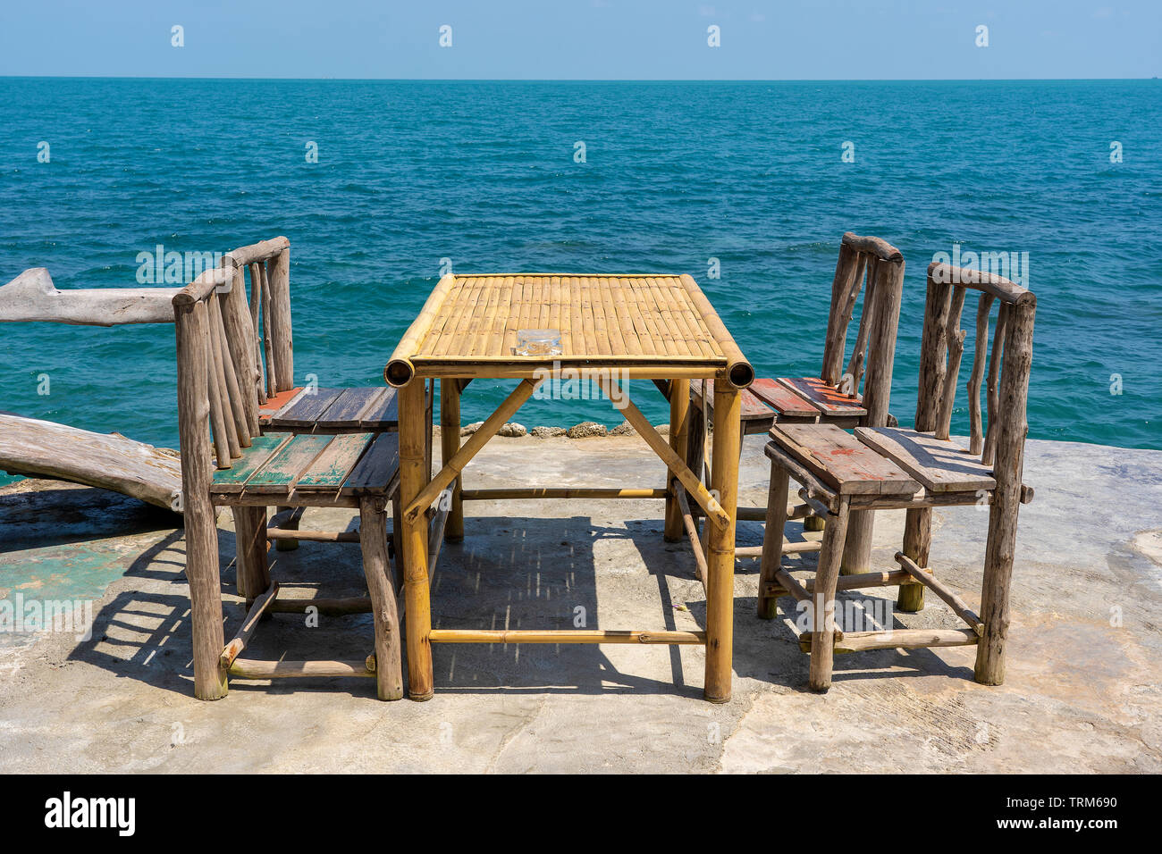 Bamboo table and wooden chairs in empty cafe next to sea water in tropical beach. Close up ...