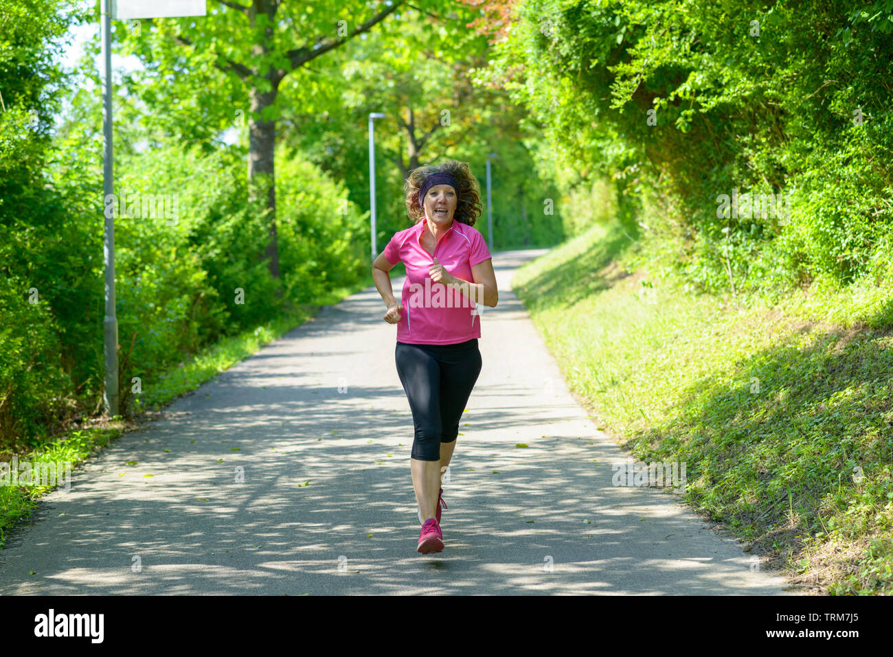 Fit middle-aged woman out jogging in spring approaching the camera ...