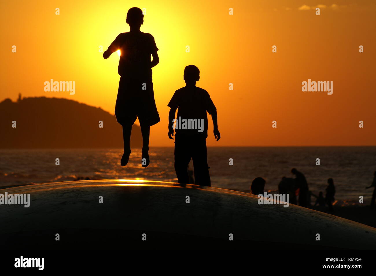 Two children jumping on a huge inflatable hill against the setting sun ...