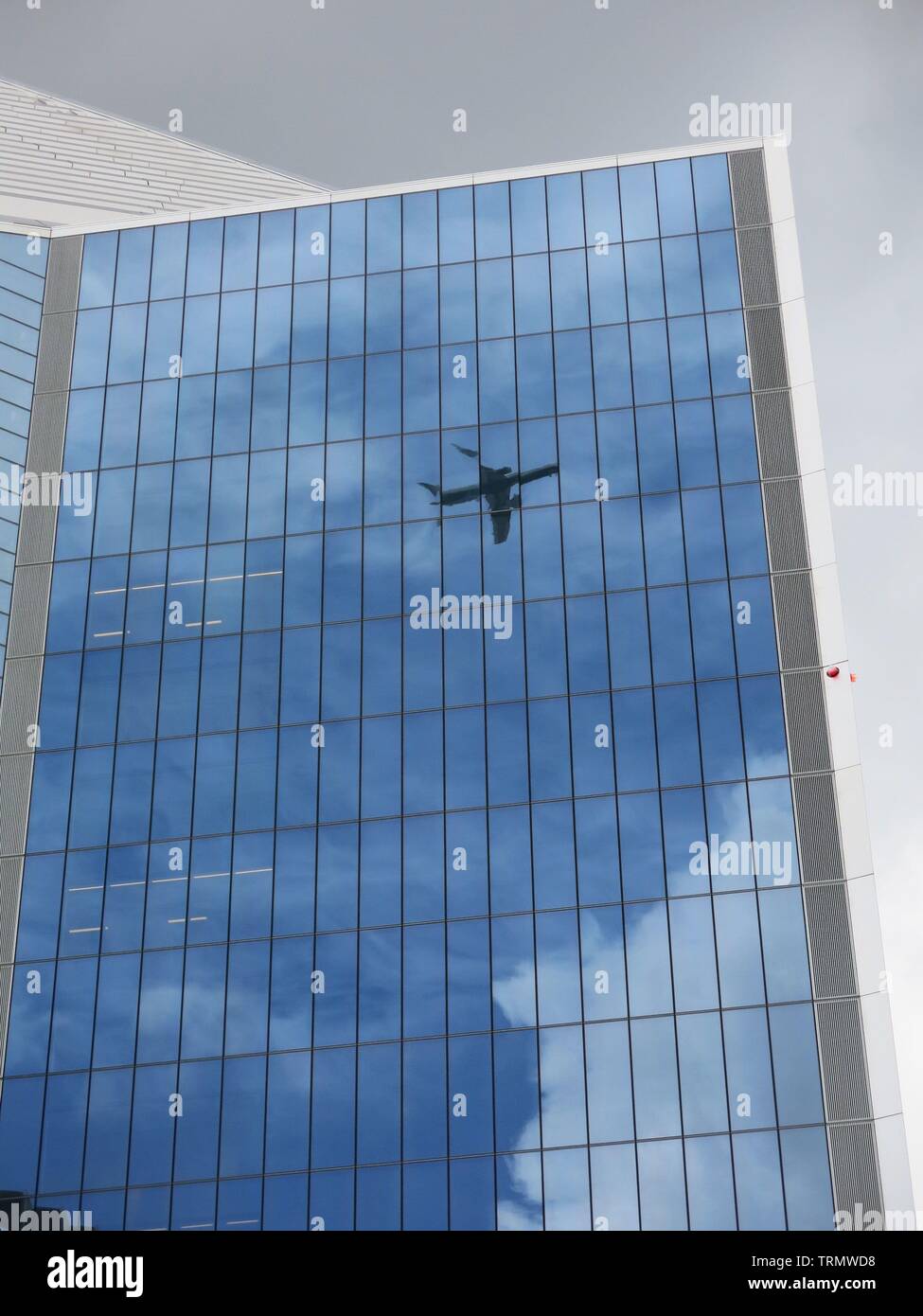An airplane flying overhead and clouds are reflected in the glass of a ...