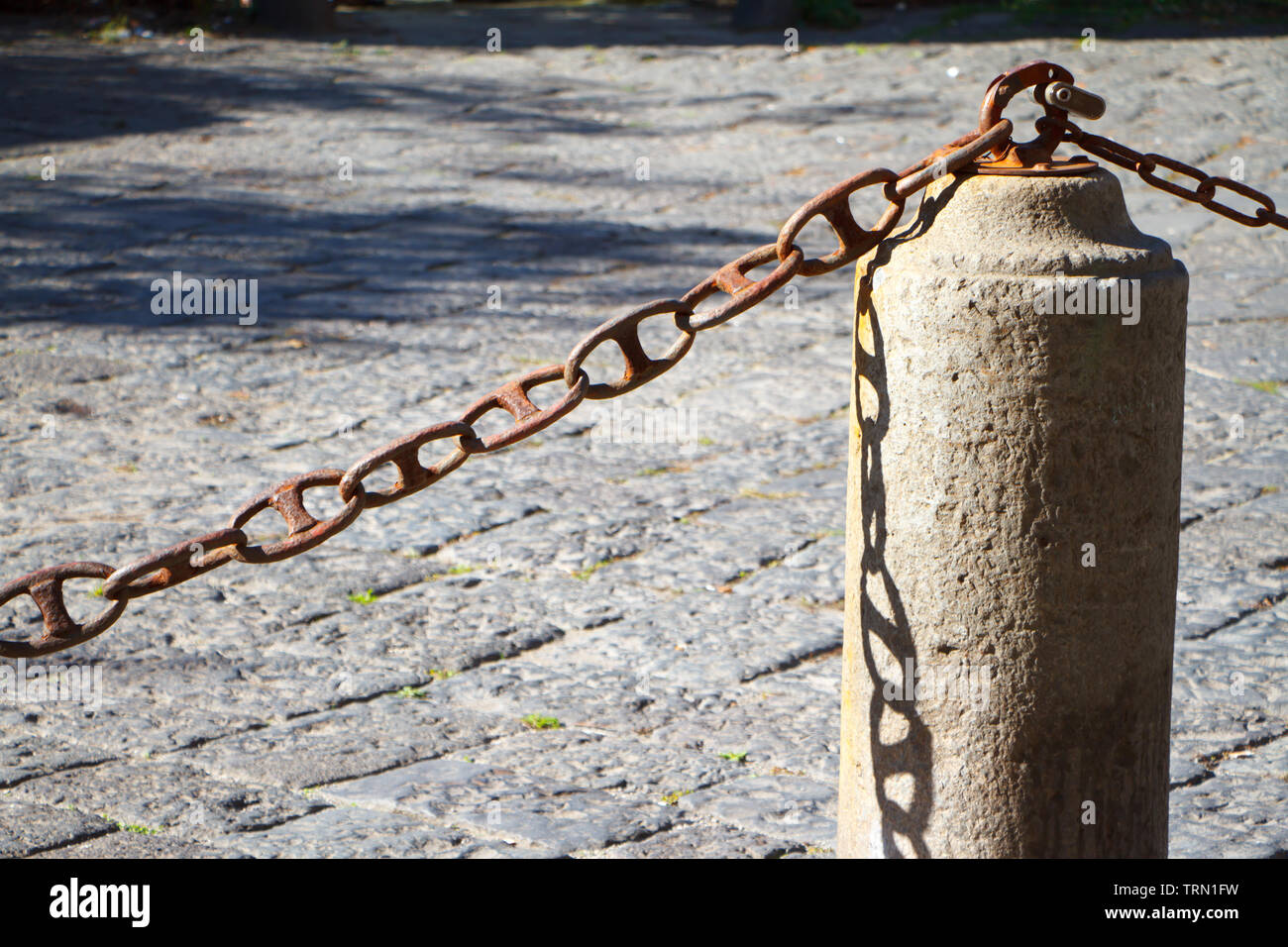 Closeup of a stone fence pillar and chain on a stone pavement ...
