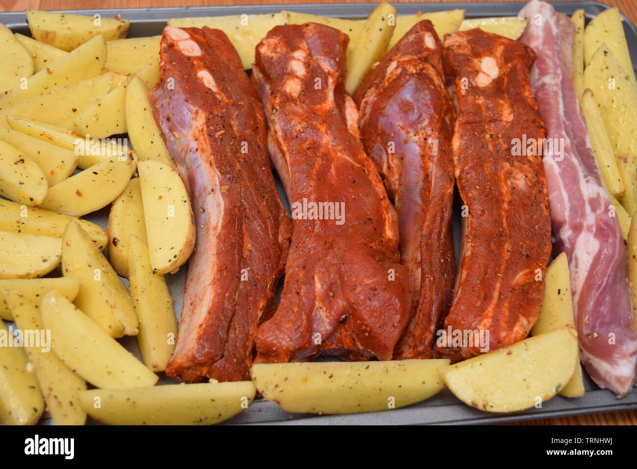 Juicy seasoned ribs with organic uncooked potato wedges on a silver ...