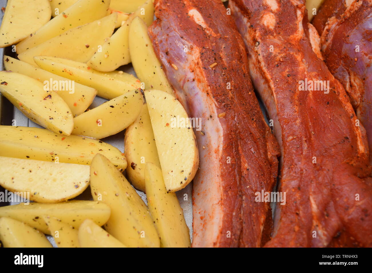 Juicy seasoned ribs with organic uncooked potato wedges on a silver ...