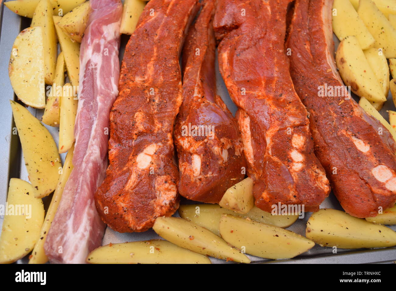 Juicy seasoned ribs with organic uncooked potato wedges on a silver ...