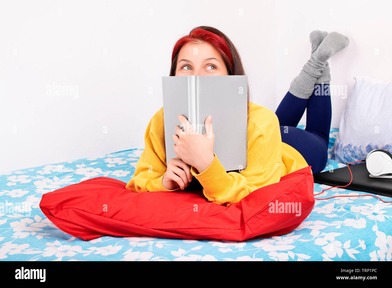 Young beautiful girl lying on the bed in a bedroom, next to a laptop ...
