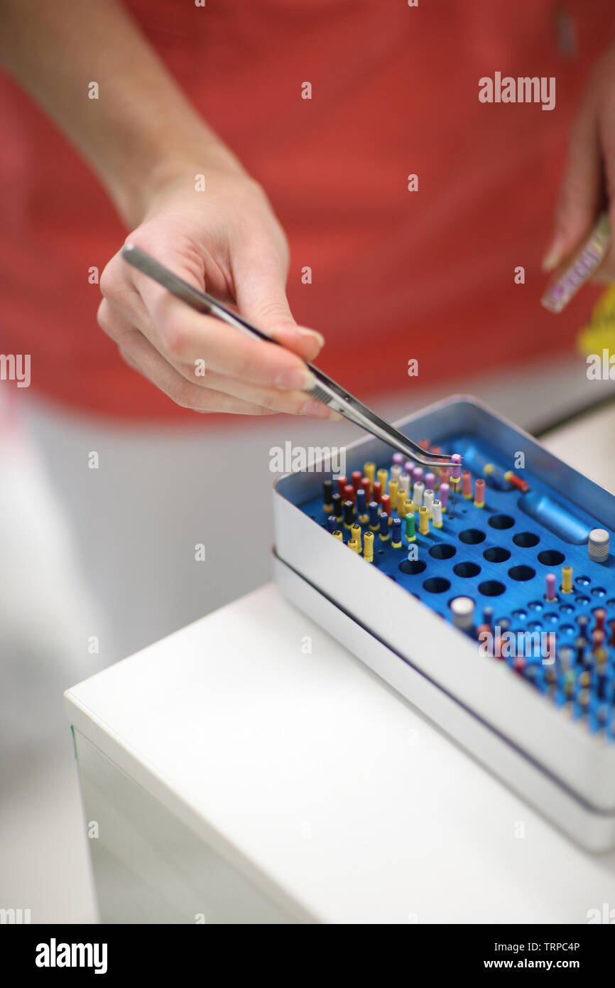 Assistant dentist with tweezers in his hand takes special needle out of ...