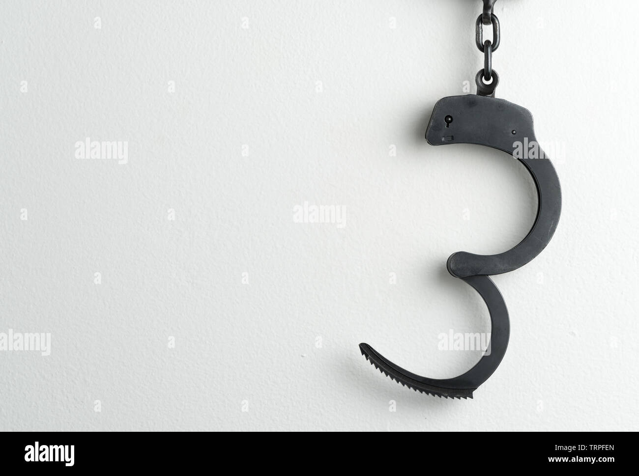 Unlocked police handcuffs on a white painted wall. Potential copy space ...
