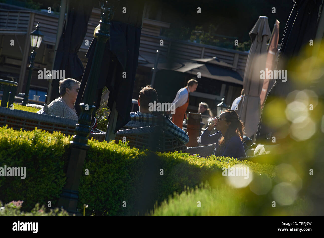 People sitting outside on a terrace in bright summer sunshine enjoying ...