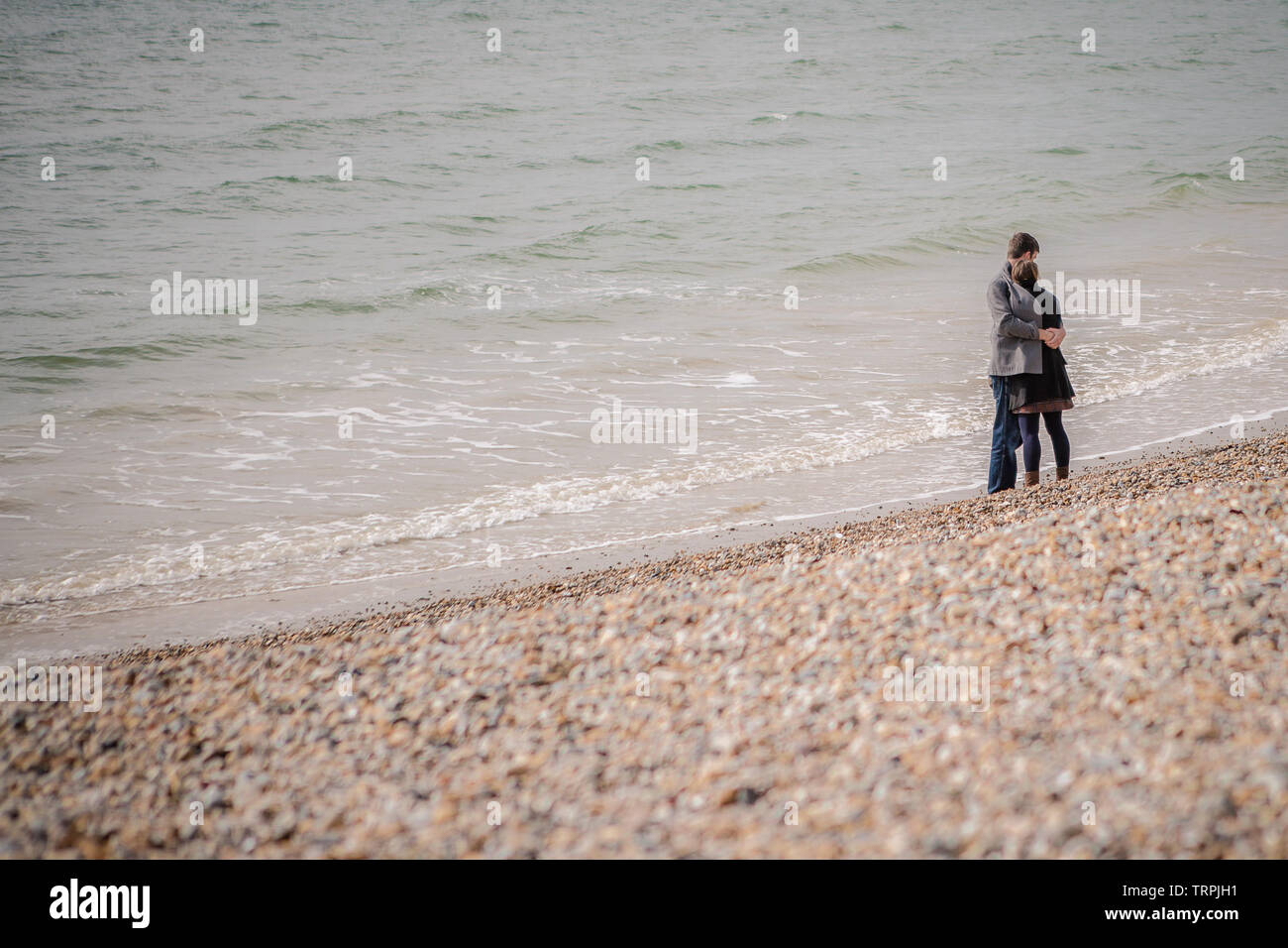 Romantic couple cuddle together on pebble beach to keep warm in cold ...