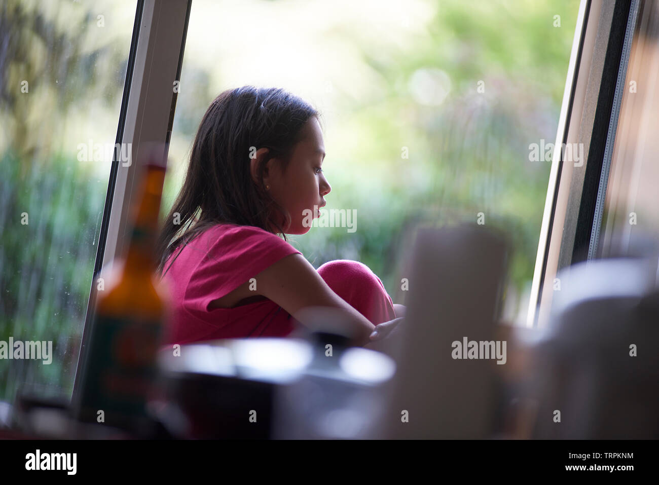 Young girl sitting on the window sill in deep thought looking upset and ...