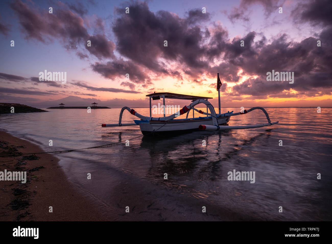 Ancient traditional Jukung fishing boat on seashore at colorful sunrise ...