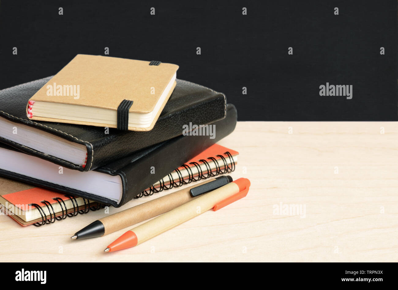 Notebooks and pens on wooden table with school black board for ...