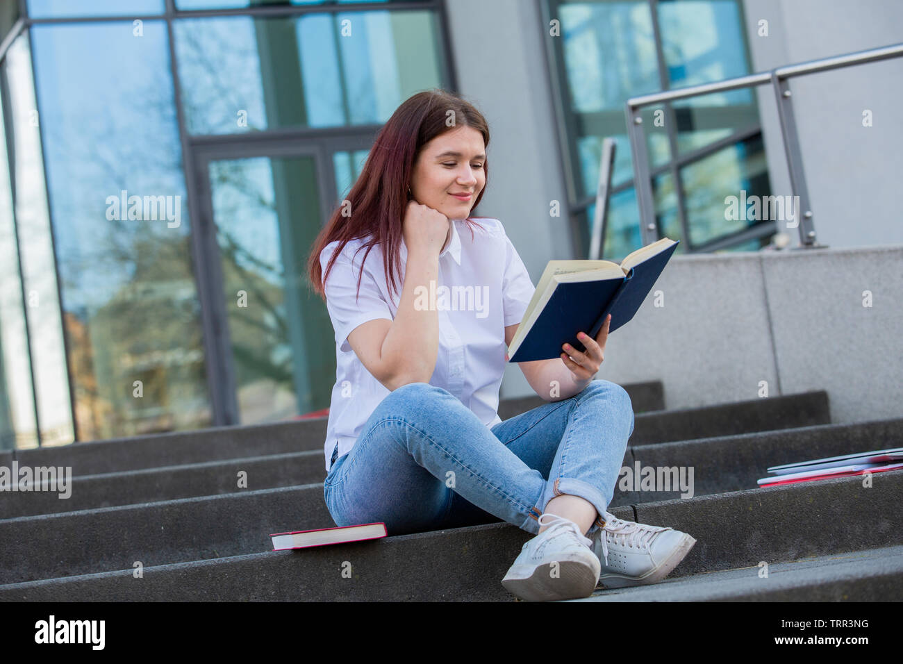 Student girl reading her favorite book outdoors on campus stairs ...