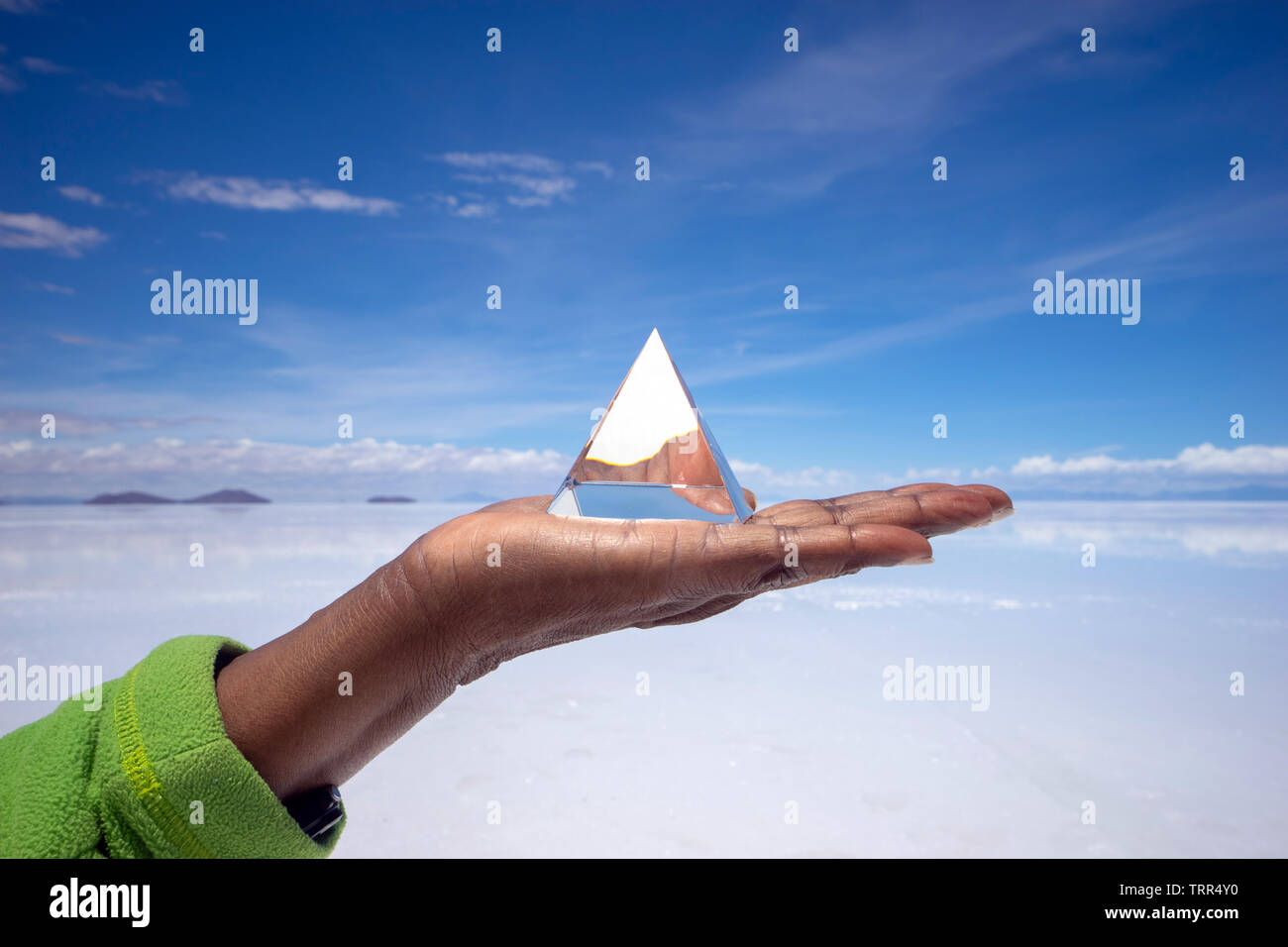Hand holding a crystal pyramid in front of a wide and sunny salt desert ...