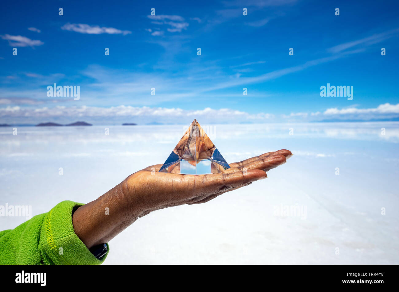 Hand holding a crystal pyramid in front of a wide and sunny salt desert ...
