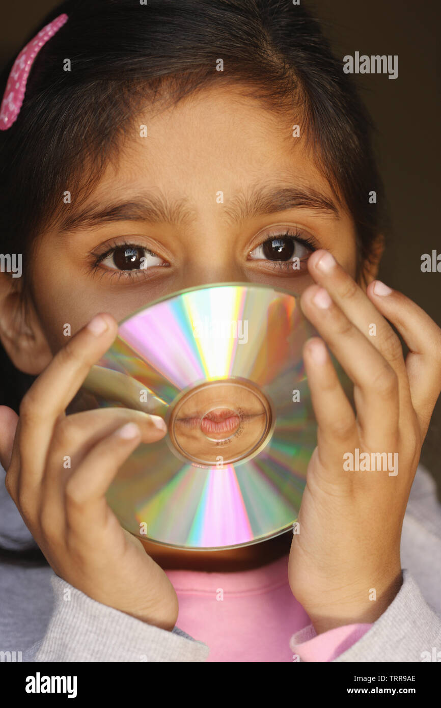Portrait of an Indian girl holding a compact disc in front of mouth ...
