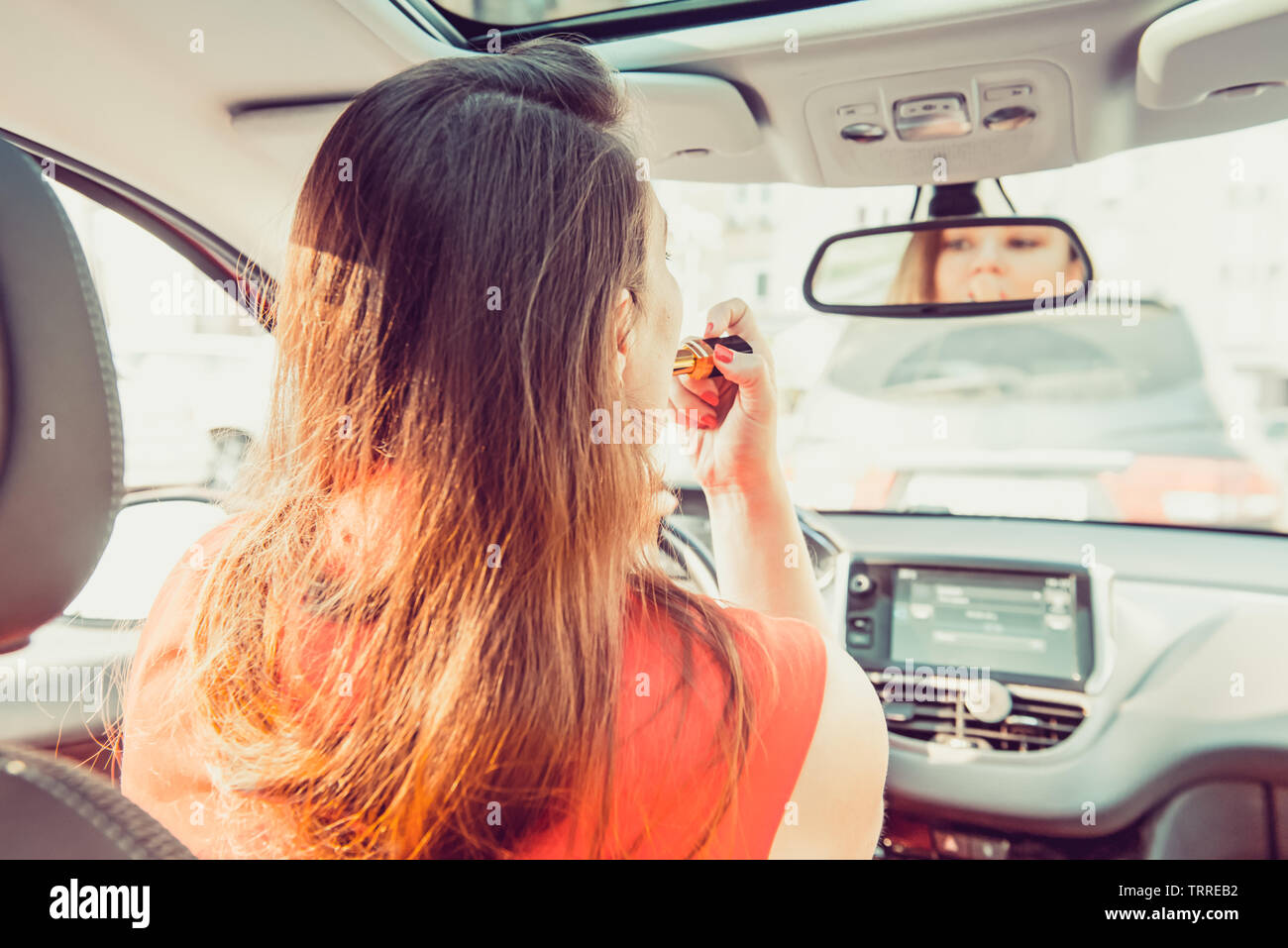 Back view young woman looking in rear view mirror and putting make up ...
