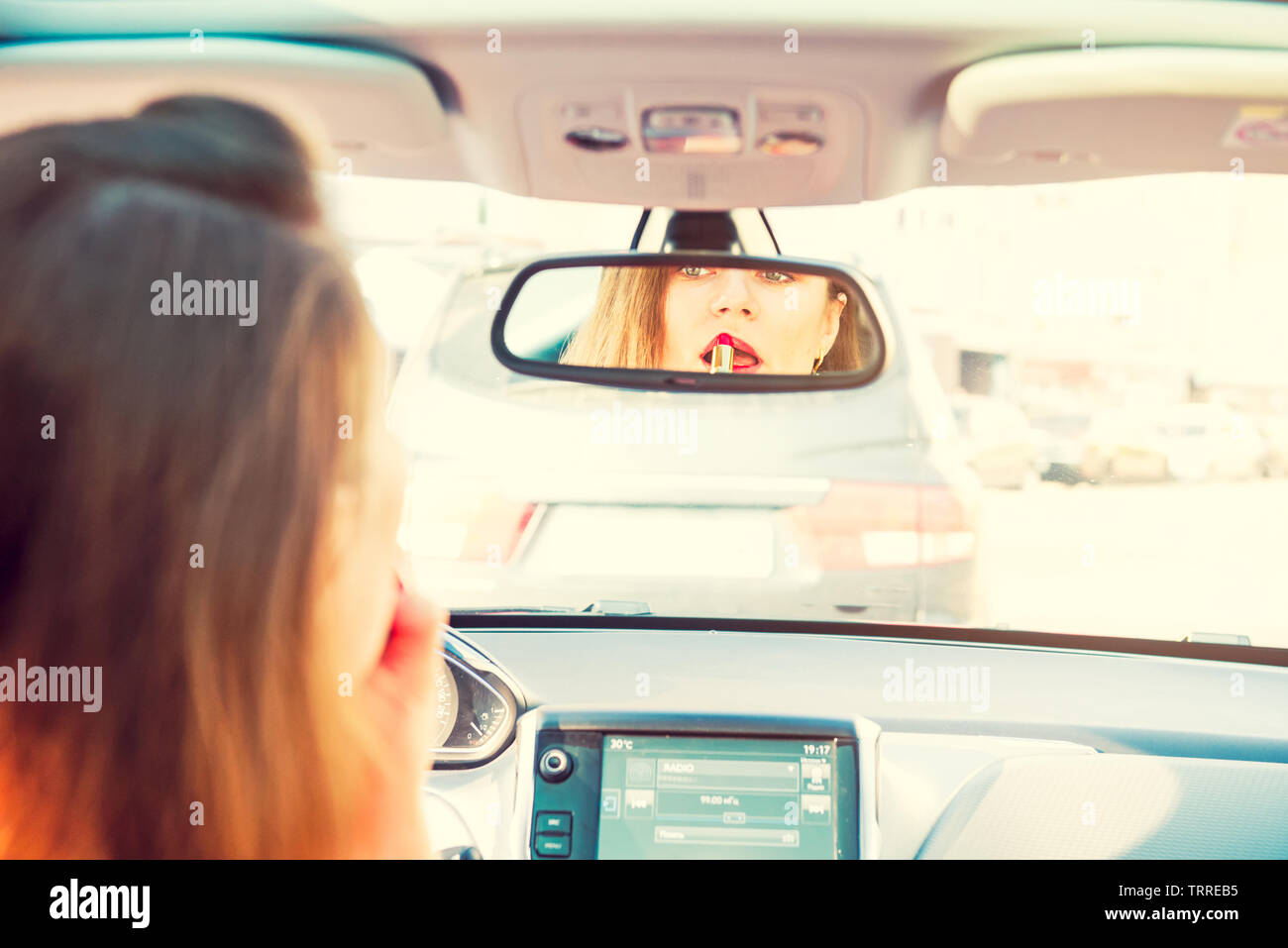 Back view young woman looking in rear view mirror and putting make up ...