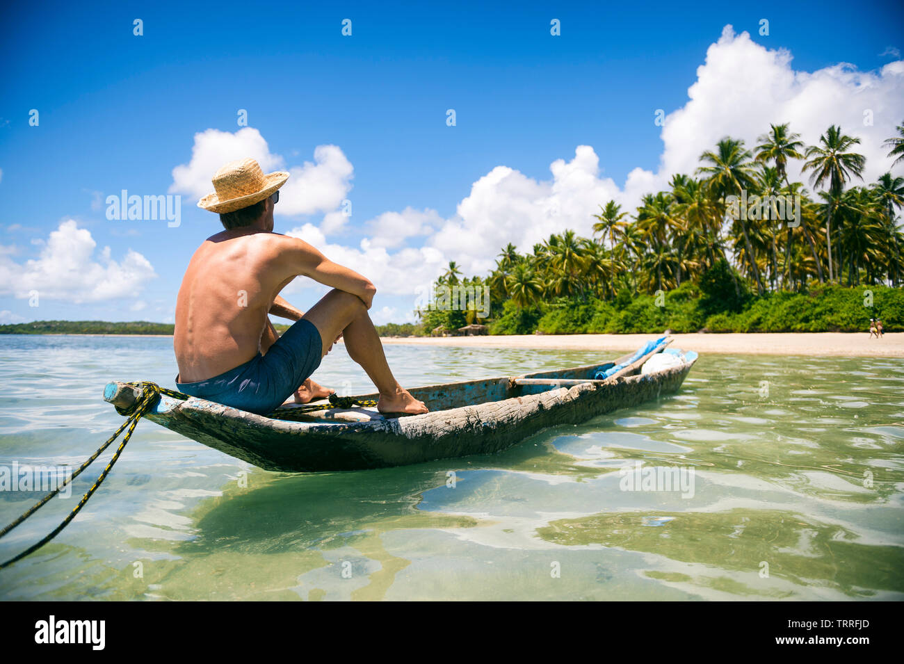 Tourist wearing a straw sun hat sitting in a rustic dugout canoe on a ...