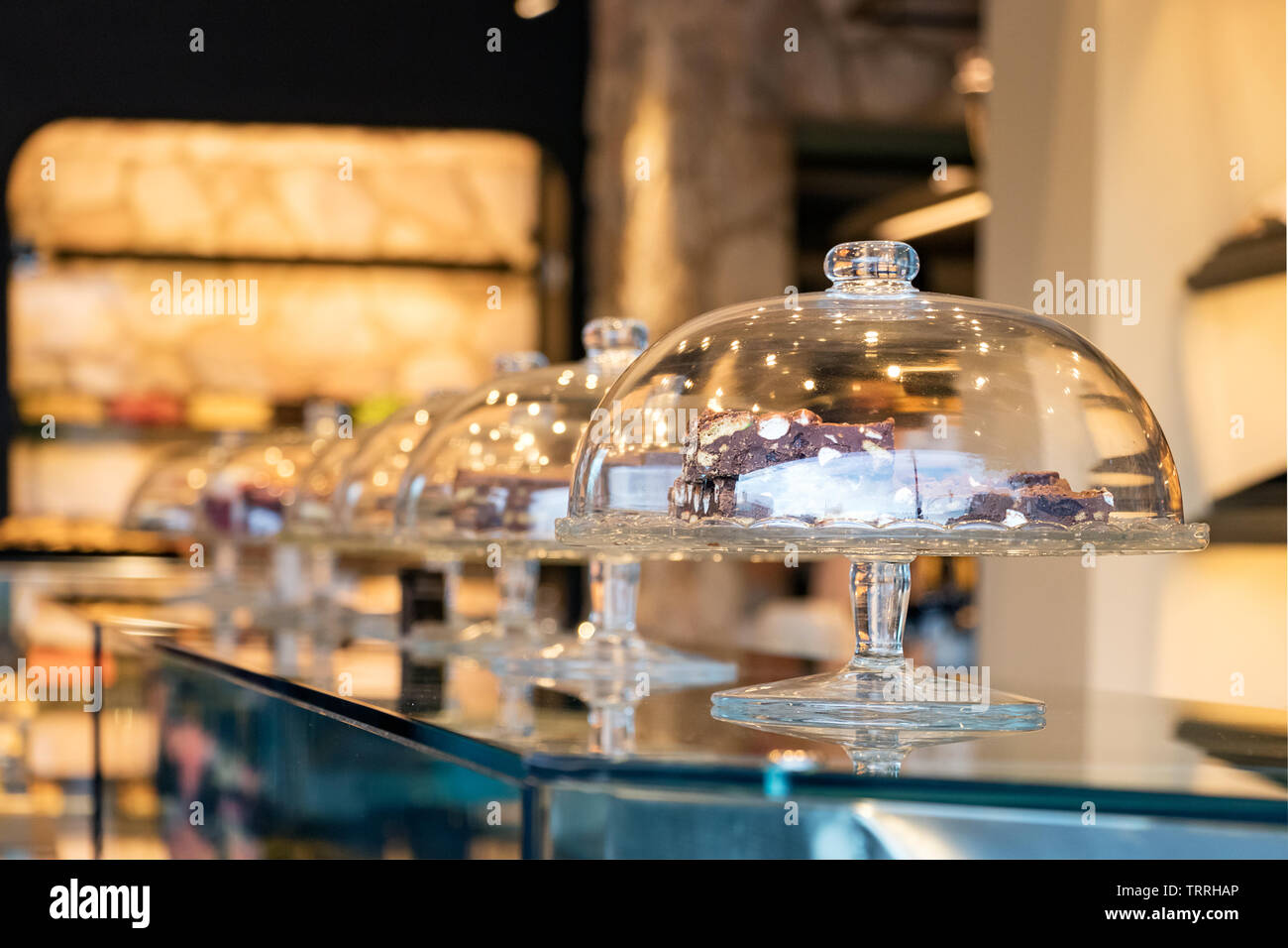 Pastry glass bells in a row placed on the counter inside a bakery store ...