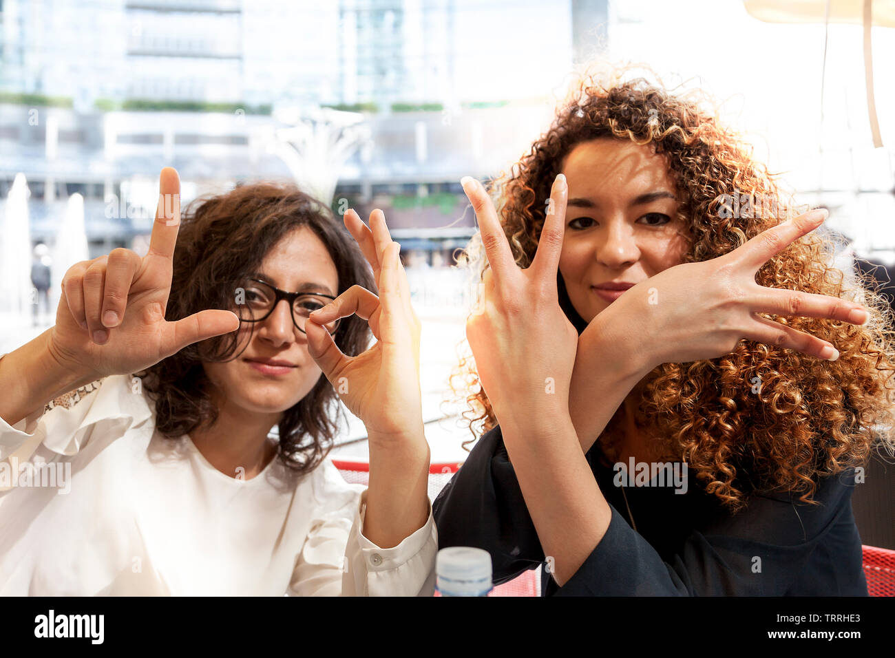 couple of pretty young woman showing symbol of love with fingers in the ...