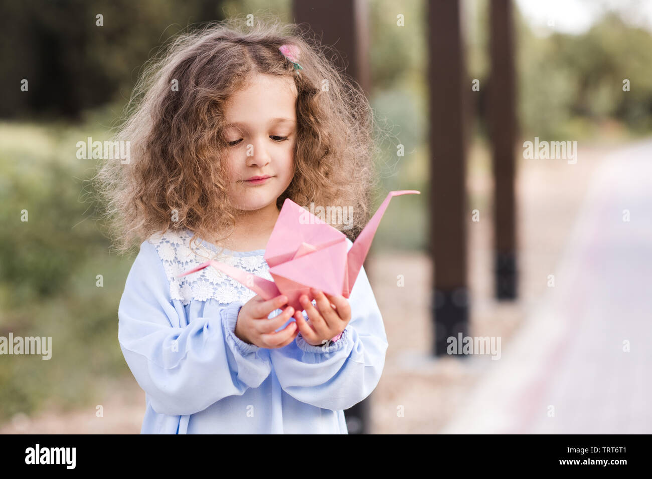 Smiling baby girl 3-4 year old holding paper origami bird in park ...
