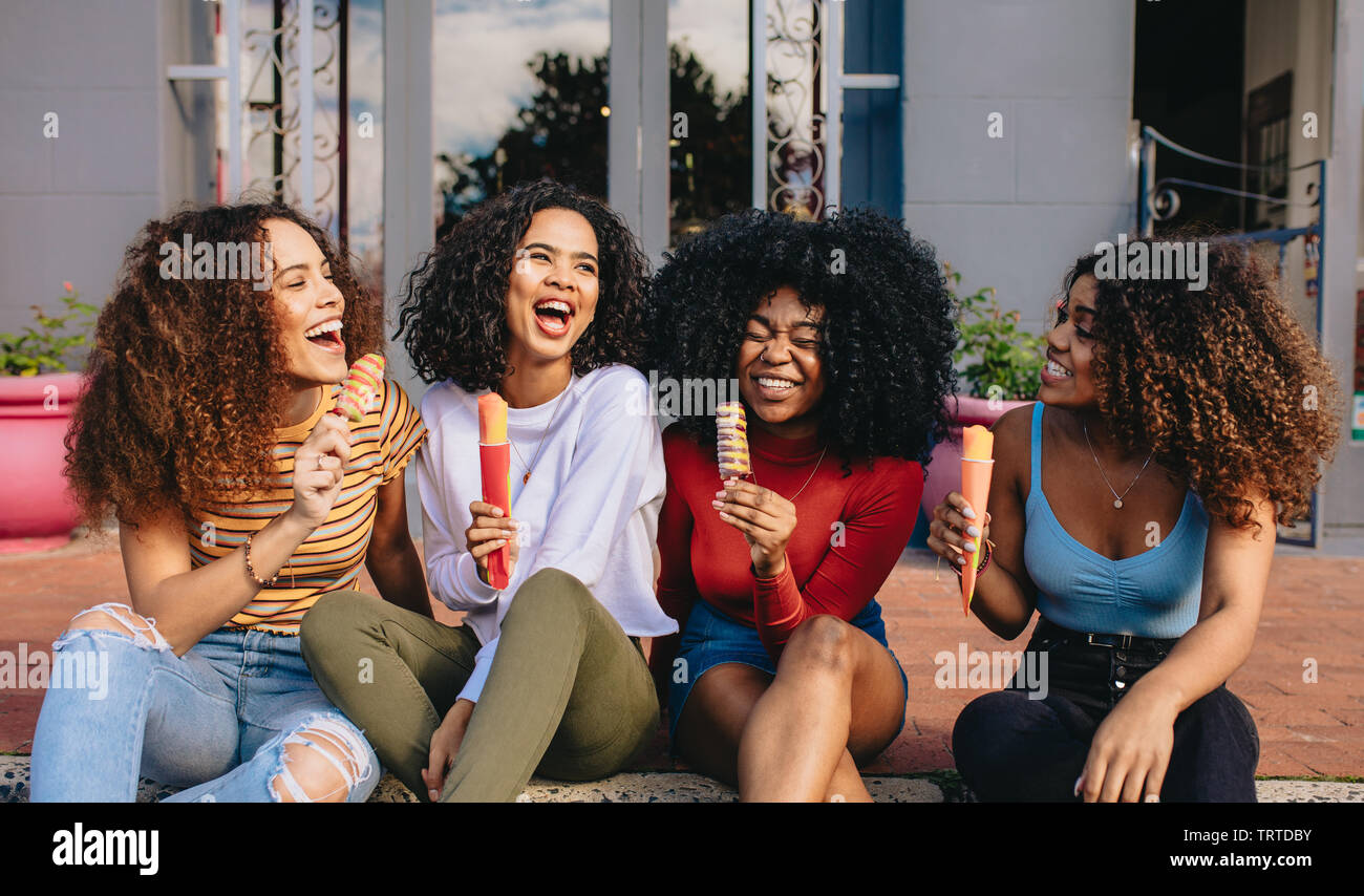 Female friends sitting outdoors enjoying eating ice cream. Group of ...